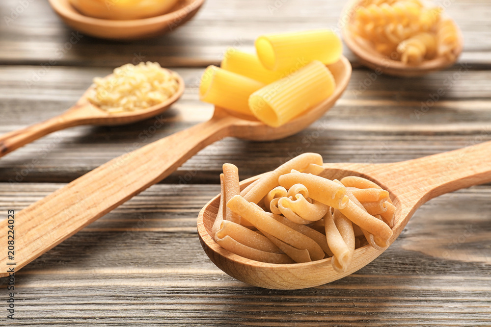 Spoons with different uncooked pasta on wooden background Stock Photo ...