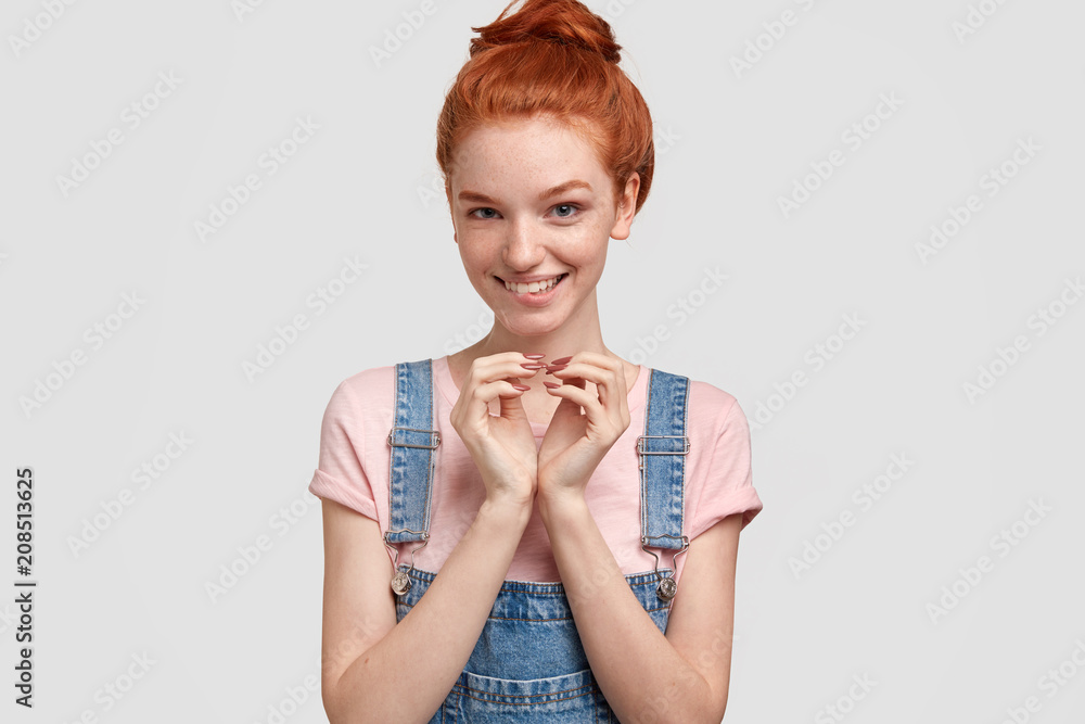 Pretty foxy female with freckled skin, keeps hands together, looks with ...