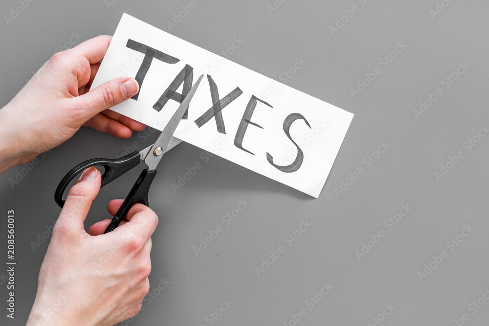 Tax reduce concept. Hands with sciccors cut paper with word Taxes on ...