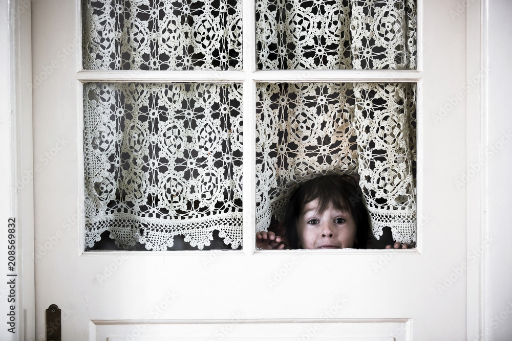 Little preschool boy, child, looking scared through a door with windows ...