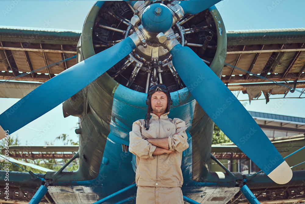 Valiant handsome pilot in a full flight gear standing with crossed arms ...