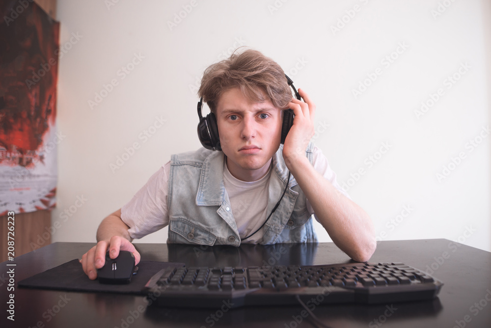 sad teenage gamer sits at home behind a computer and plays video games ...