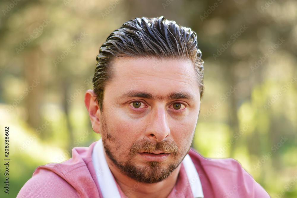 Young man's outdoors portrait looking at the camera with natural green ...
