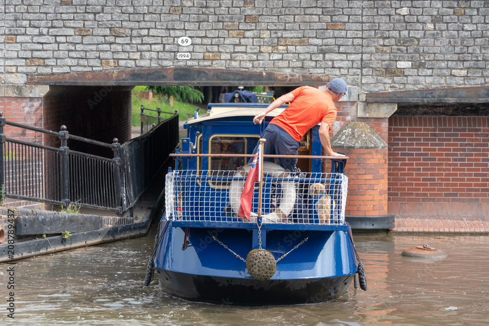 blue and cream canal boat being driven through small gap in tunnel ...