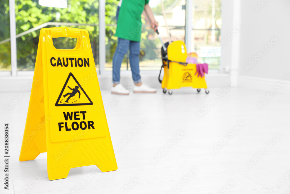Safety sign with phrase "CAUTION WET FLOOR" and young woman cleaning ...