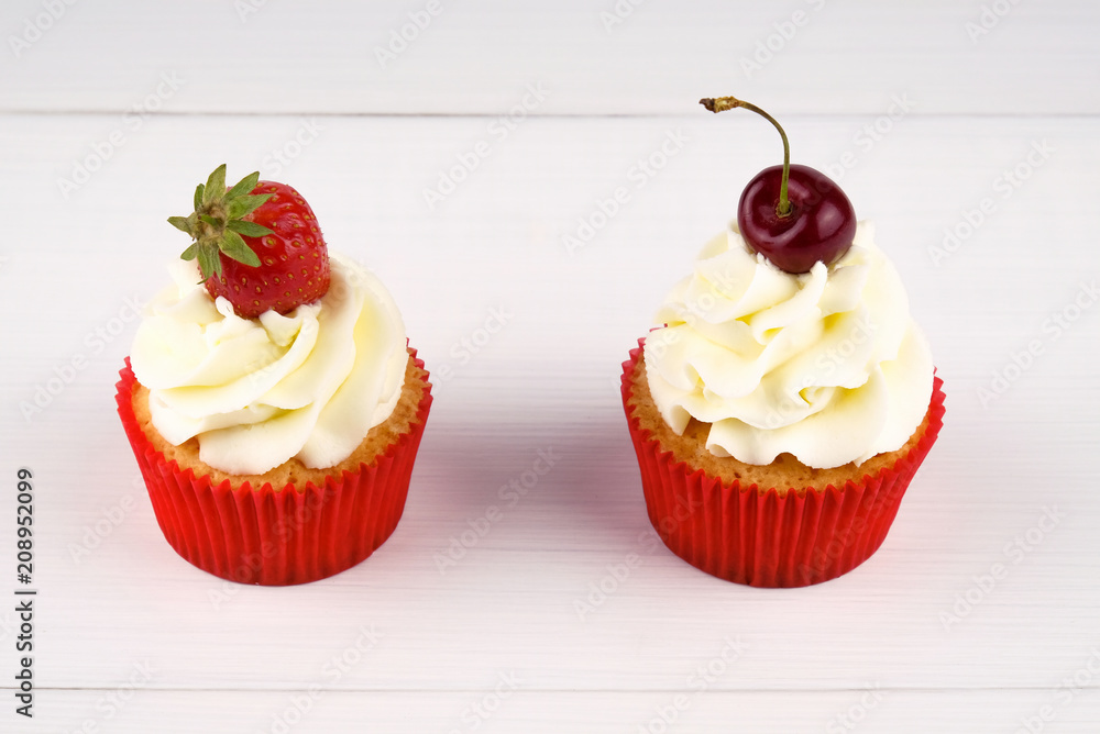 Two red cupcakes with white cream decorated with strawberry and cherry ...