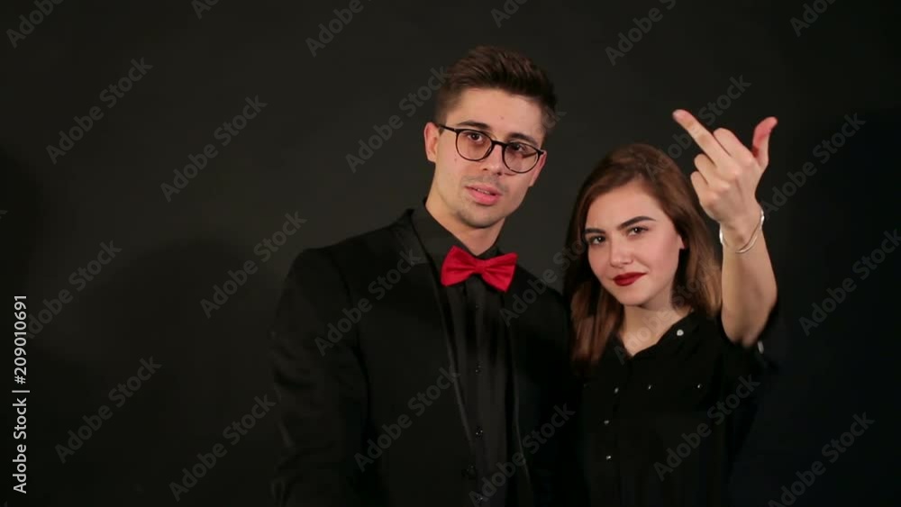 Cheerful young couple of hipsters showing middle finger against a black ...