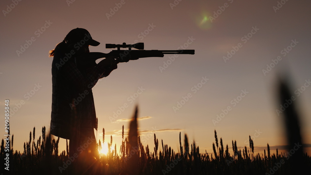 The hunter is aiming from a rifle with an optical sight. It stands in a ...