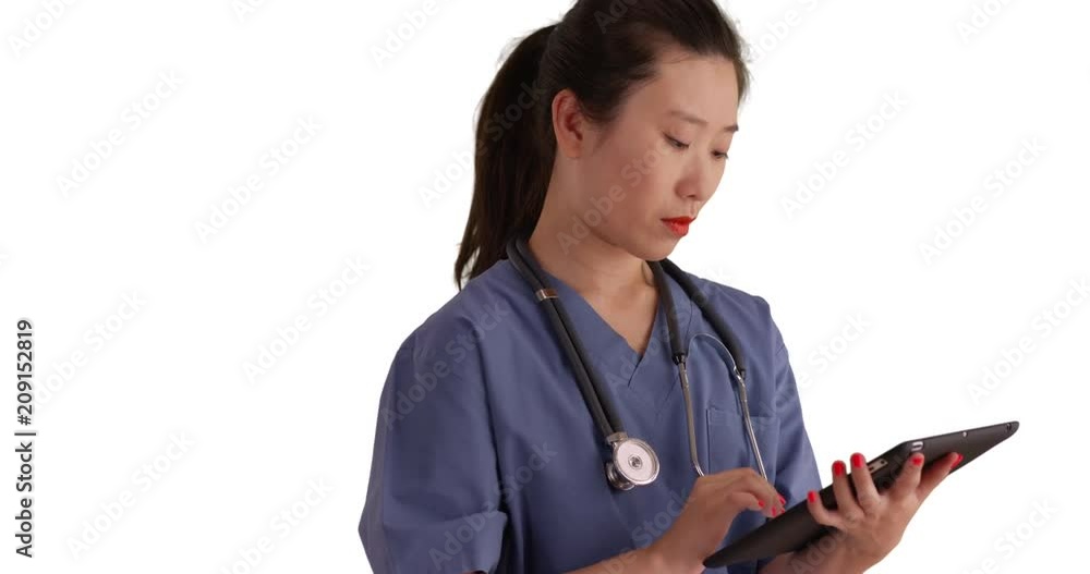 Working millennial nurse dressed in scrubs using handheld tablet device ...