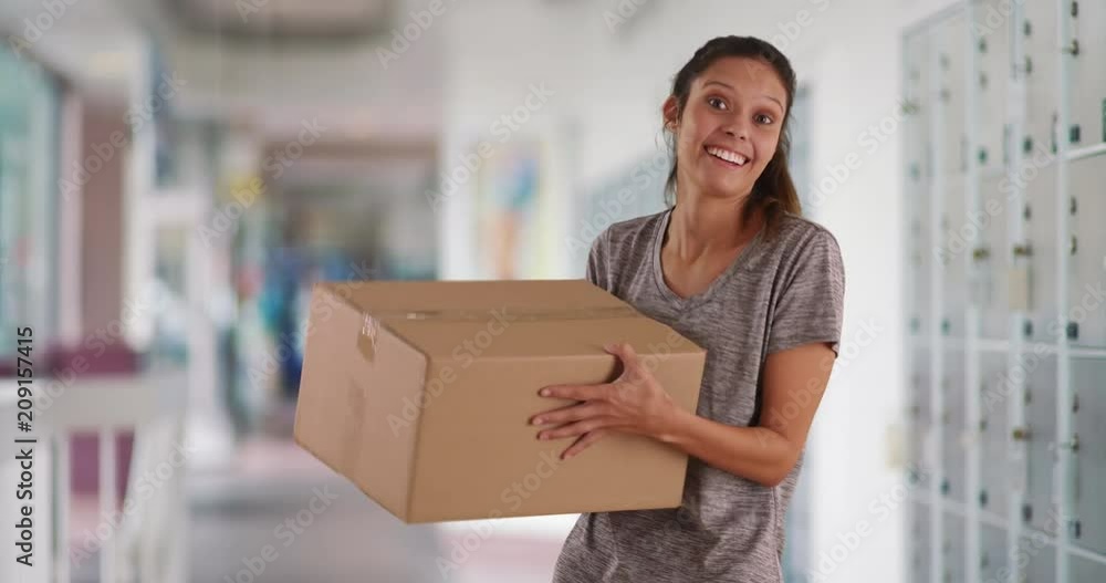 Cheerful young woman at post office tossing cardboard box into air ...