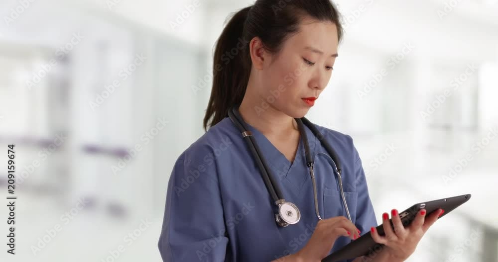 Working millennial nurse dressed in scrubs using handheld tablet device ...