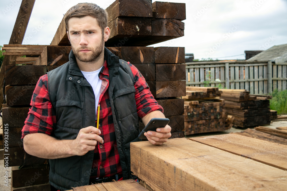 Lumber yard worker, carpenter at wood yard counts inventory with mobile ...