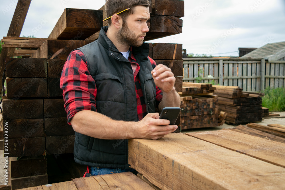 Lumber yard worker, carpenter at wood yard counts inventory with mobile ...