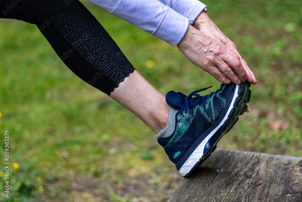 Female baby boomer in running gear stretching out a leg on a wood bench ...