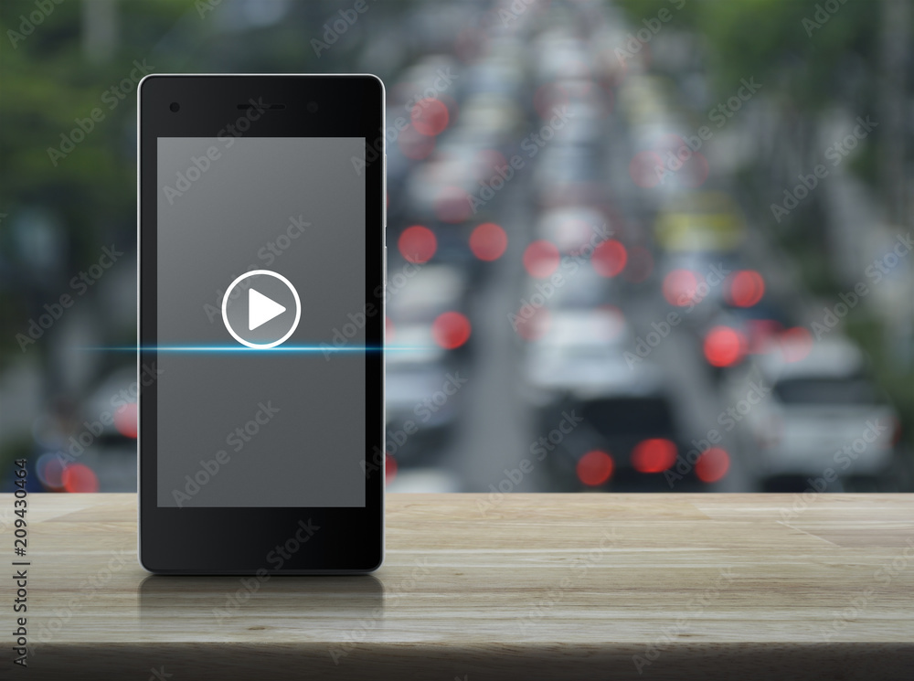 Play button on modern smart phone screen on wooden table over blur of ...
