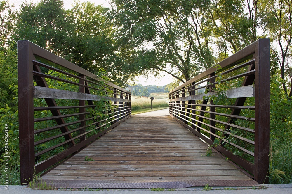 wood and steel bridge on walking path over stream around small lake ...