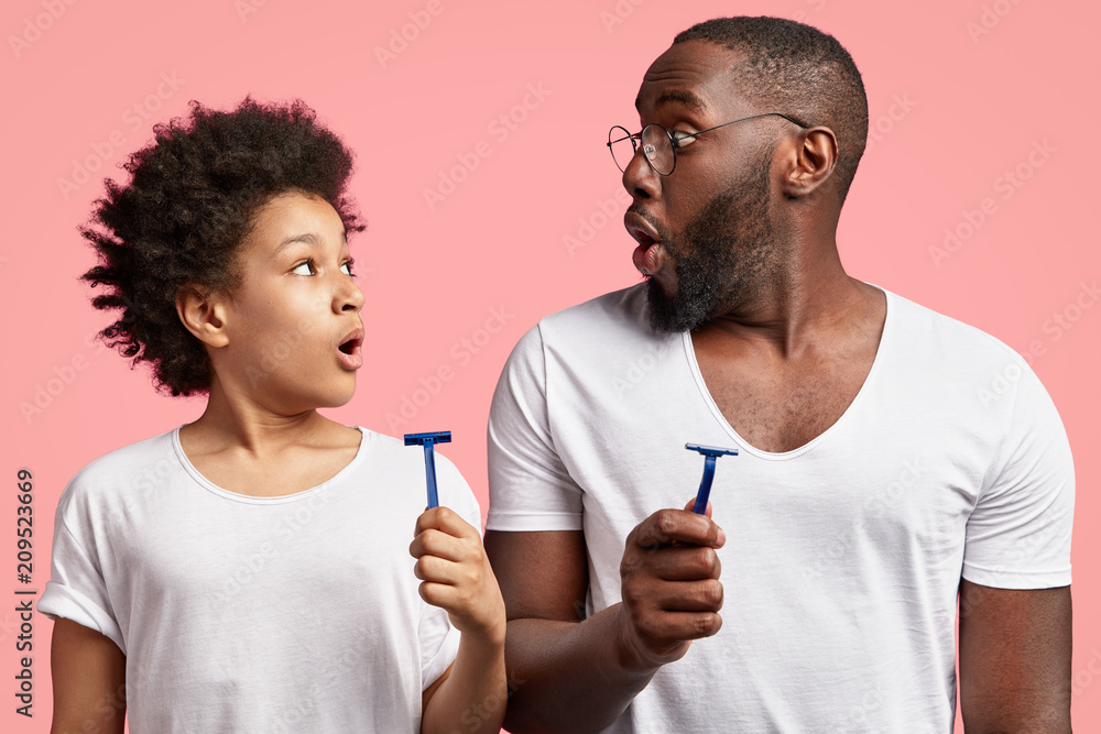 Studio shof of surprised dark skinned father and his male child, hold ...