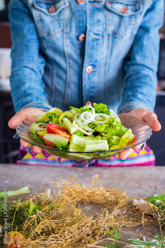 Woman hands holds fresh vegetables salad on legs. With cucumbers ...