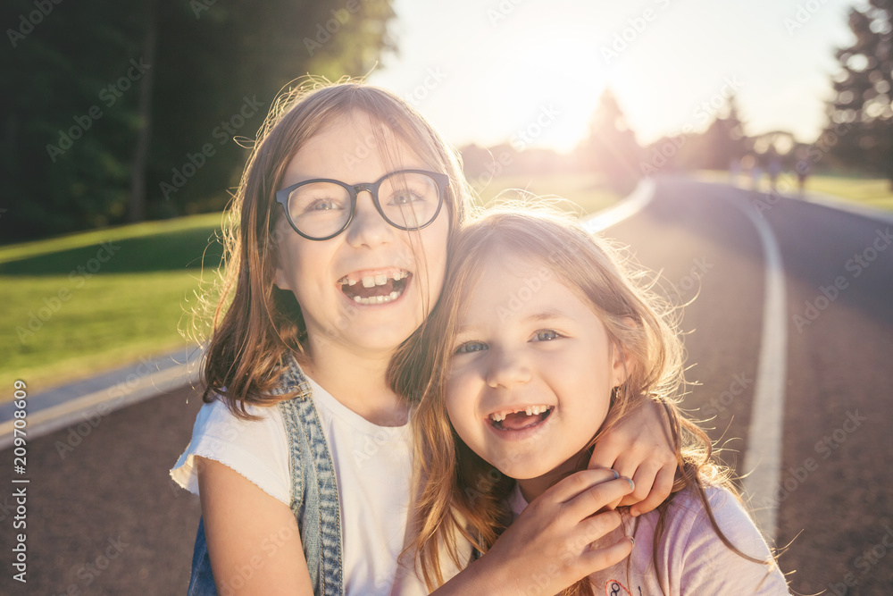 Two joyfull girls standing on the road, hugging and smiling against the ...