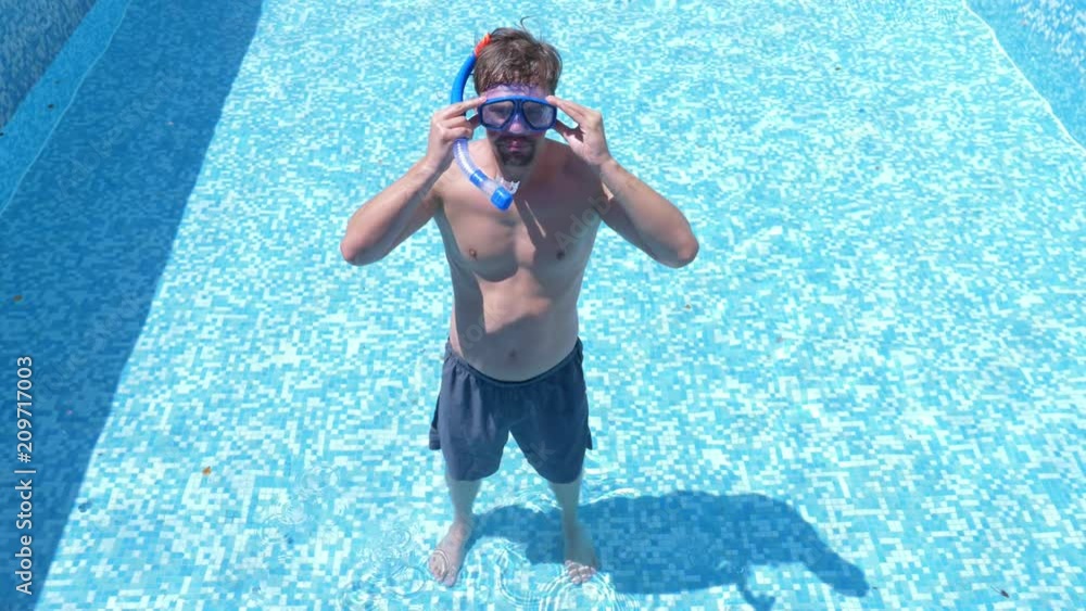 a young funny guy climbs into an empty swimming pool with a snorkelling ...