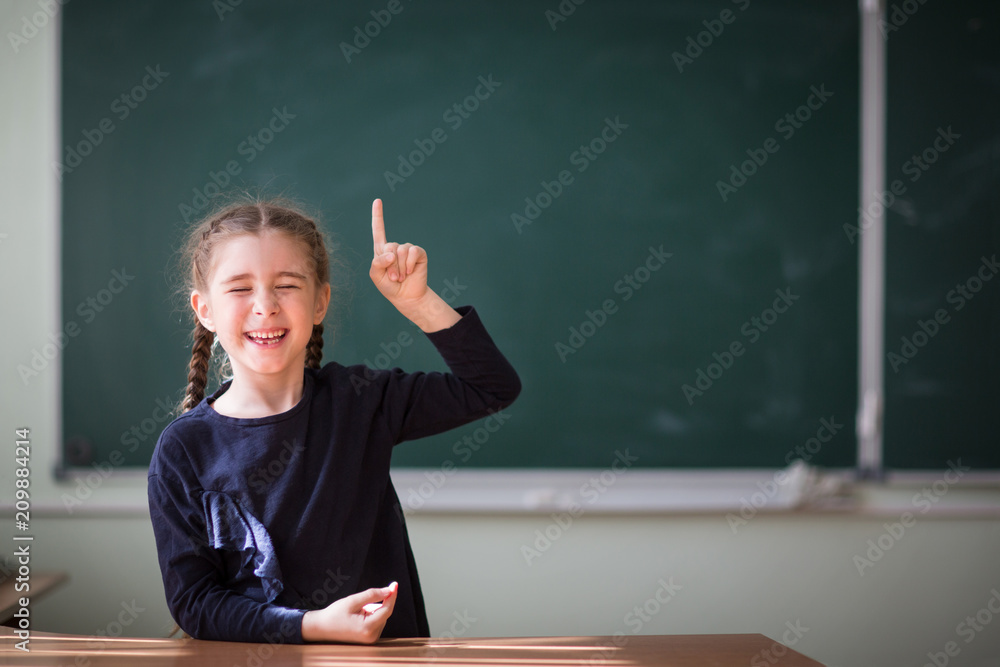 girl raised an index finger and laughing in front of a green school ...