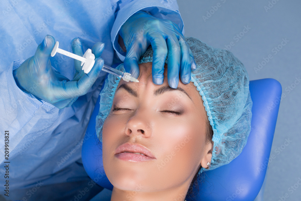 Doctor giving face lifting injection on woman in the forehead between ...