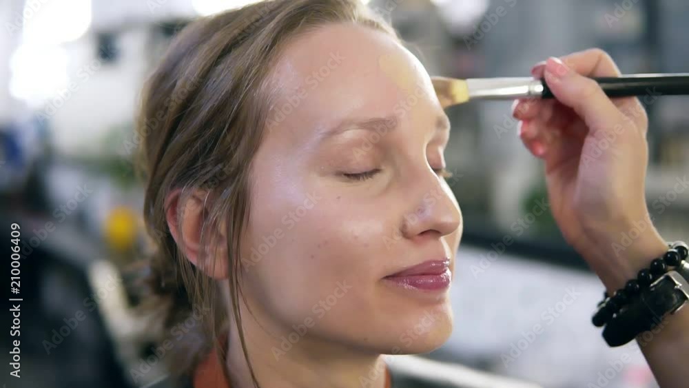 Close up of face of young woman getting base on her face with a brush ...