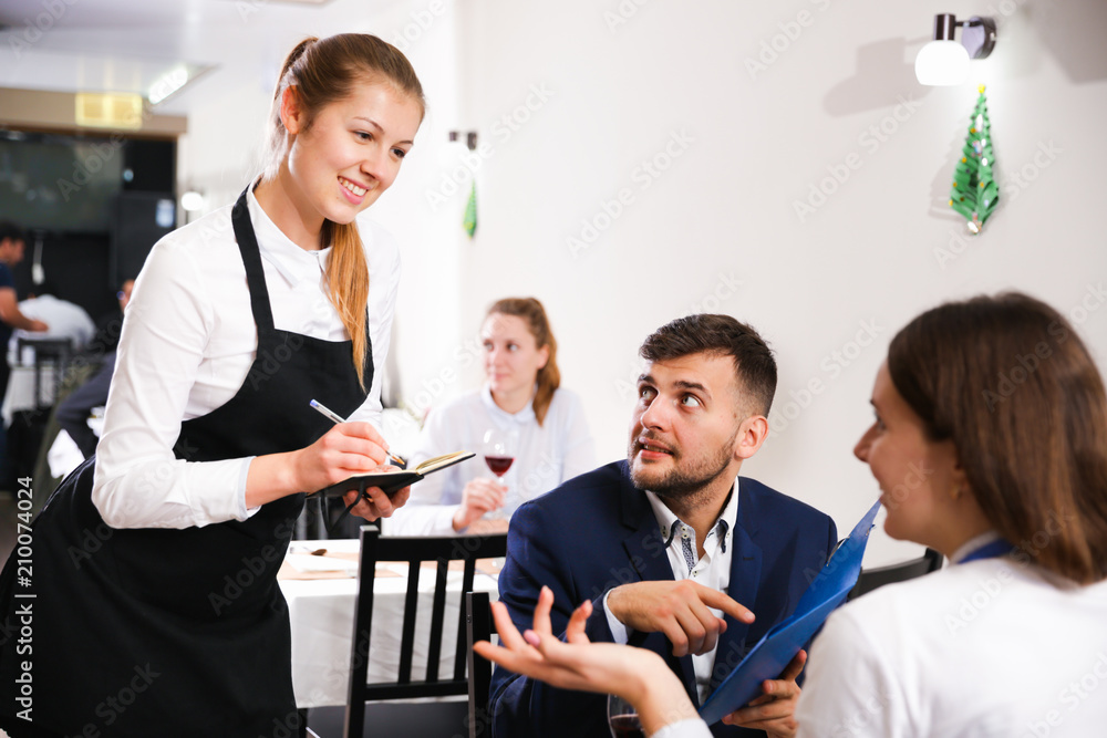 Welcoming female waiter is taking order from couple in restaurante ...