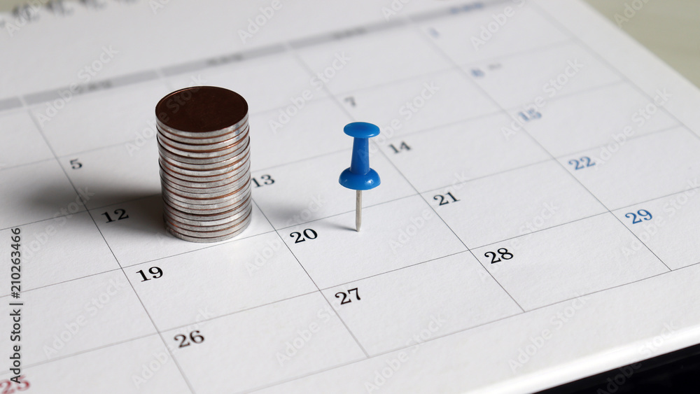 A pile of coins and a blue tack on the calendar. Stock Photo | Adobe Stock