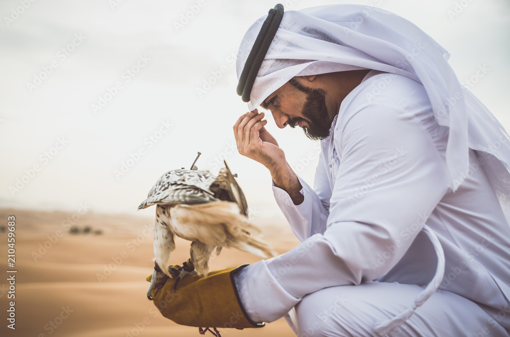 Arabic man with traditional emirates clothes walking in the desert with ...