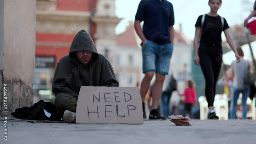 Homeless man sitting on a street with sign woman gives food people walk ...