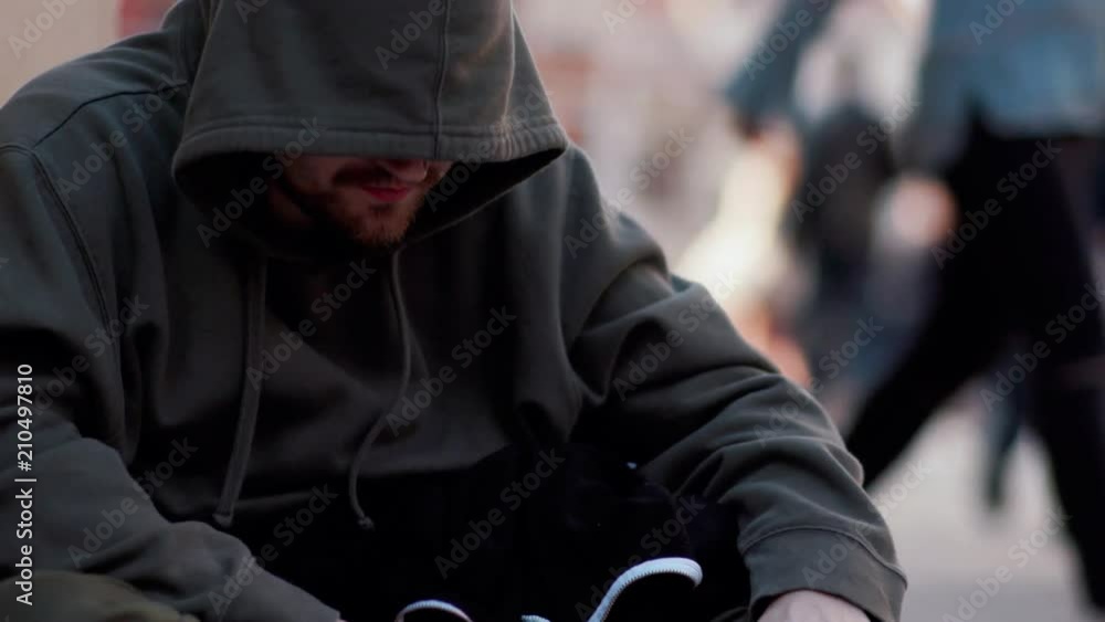 Close up homeless man sitting on street with sign eating people walk ...