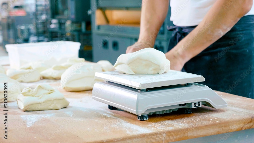 Professional baker divides the dough into portions and weights them ...