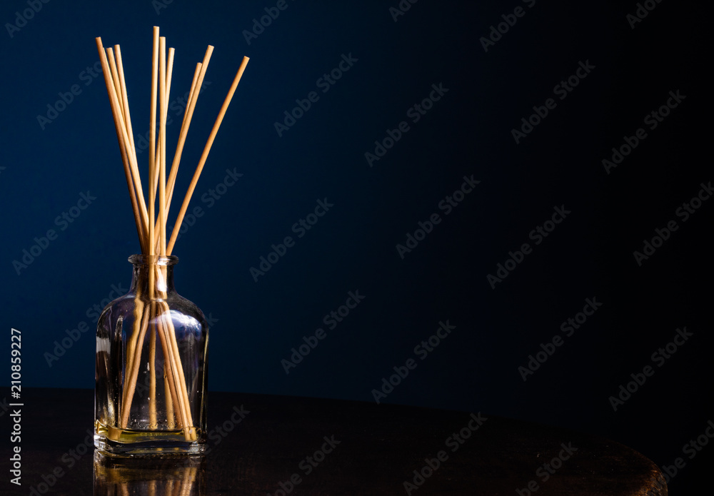 Reed diffusers in a small glass bottle on a table with a navy blue ...