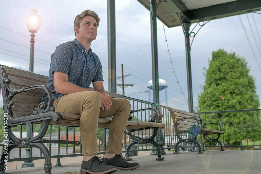 Young man happily sits on park bench with a beaming light pole lighting ...