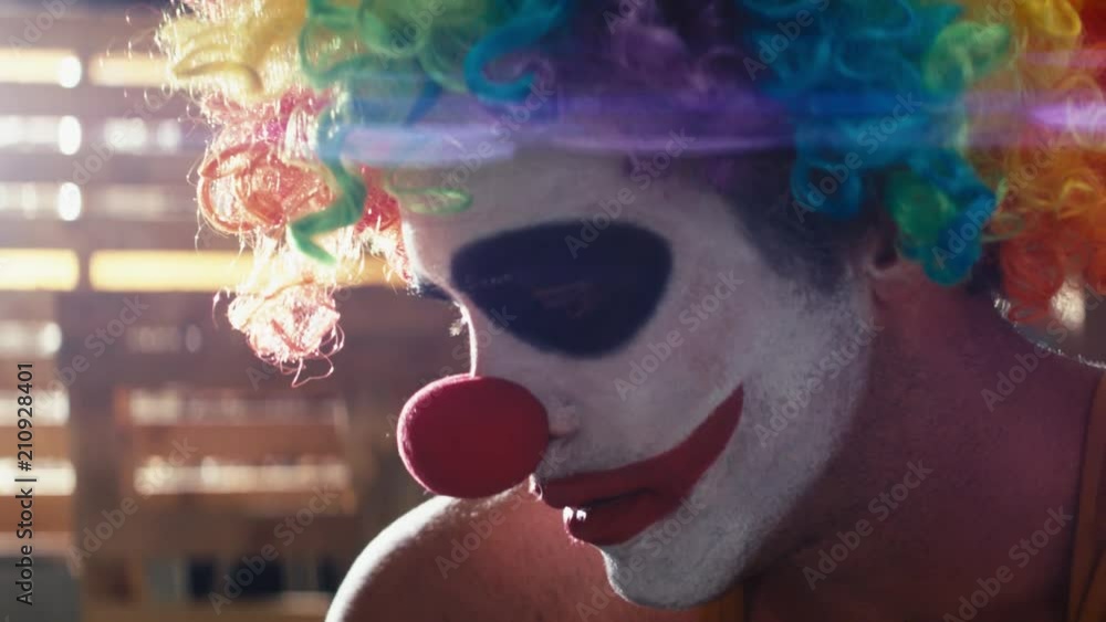 Close up sad crazy clown smoking a cigarette with anamorphic lens flare ...