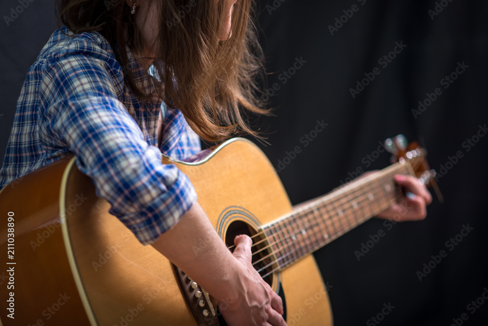 Girl teenager playing an acoustic guitar on a dark background in the ...