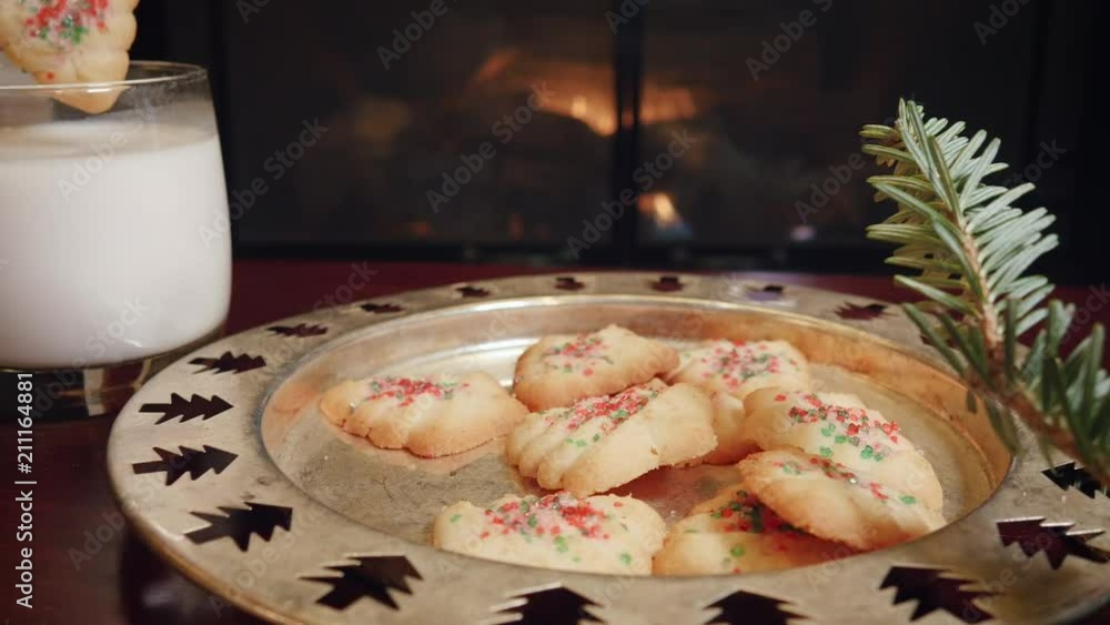 Woman grabs a christmas cookie off a plate and dips it in a glass of ...