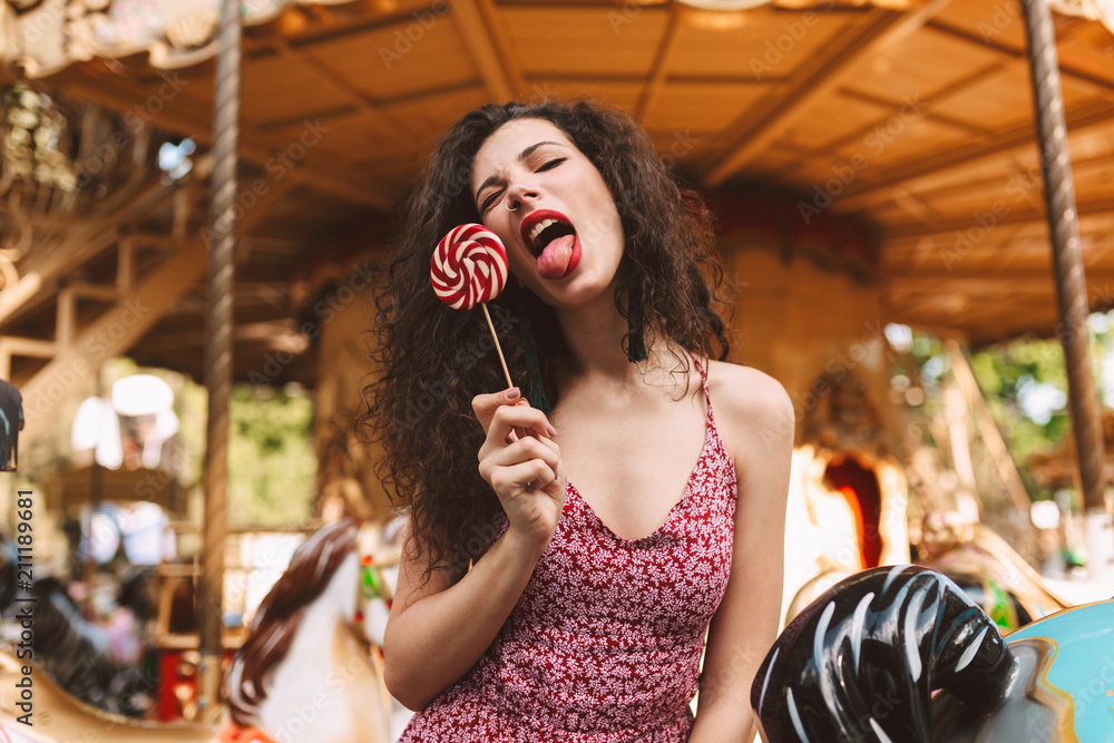 Young cool lady with dark curly hair in dress standing with lolly pop ...