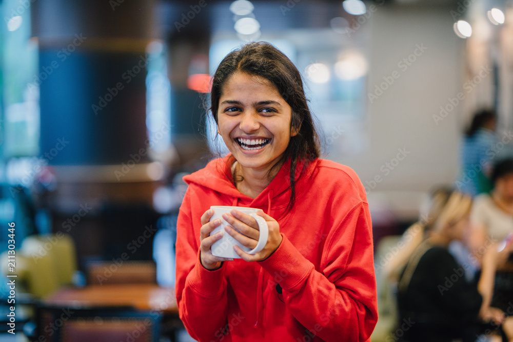 A happy youthful Indian lady laughing and enjoying a coffee in a cafe ...