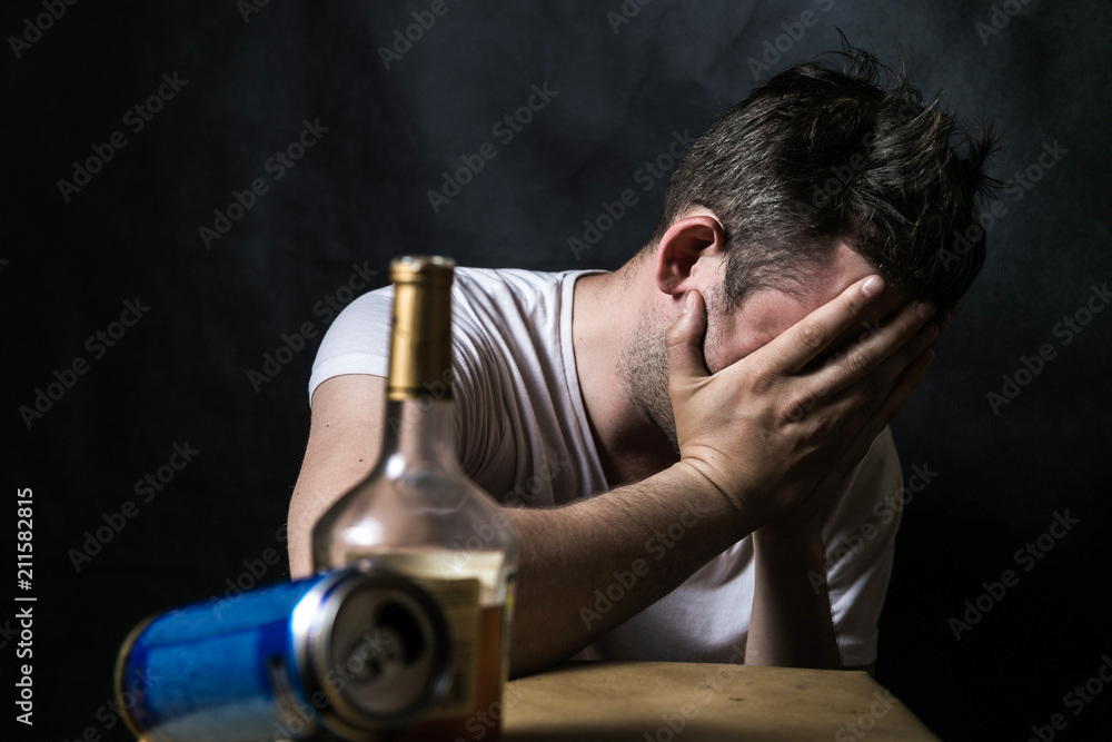 bottle of alcohol with drinking man. Serious unhappy sad man sitting ...