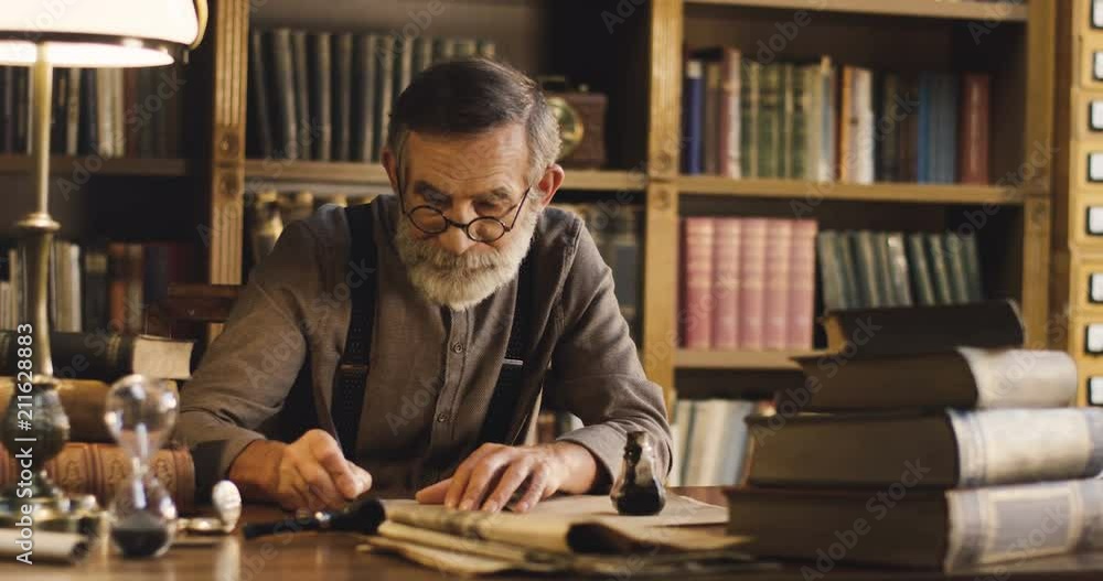 Portrait of the old man with gray beard and in glasses writing a letter ...