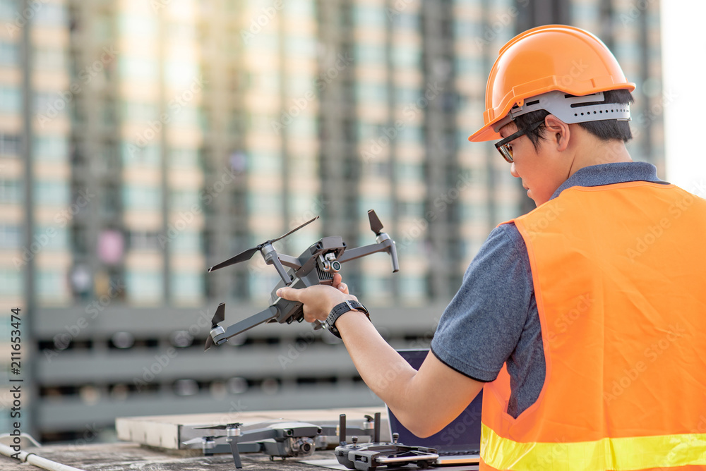 Young Asian engineer holding drone at construction site. Using unmanned ...