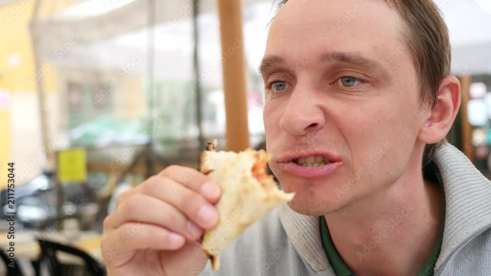 Young man guy eating chewing a piece of pizza in Rome street restaurant ...