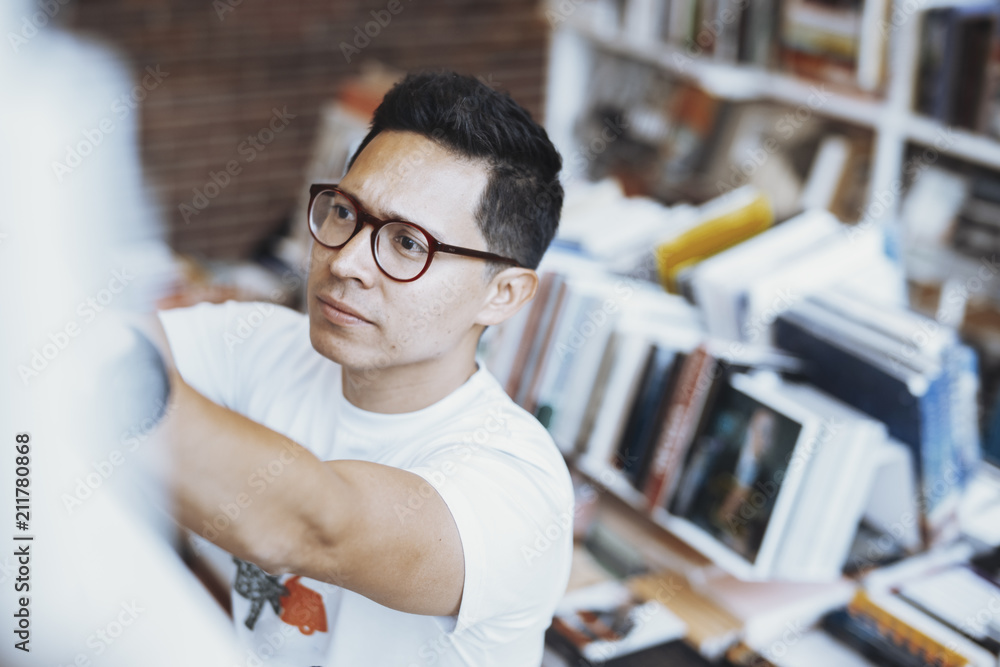 Young atrractive spectacled man drawing hand to book on a book shelf ...