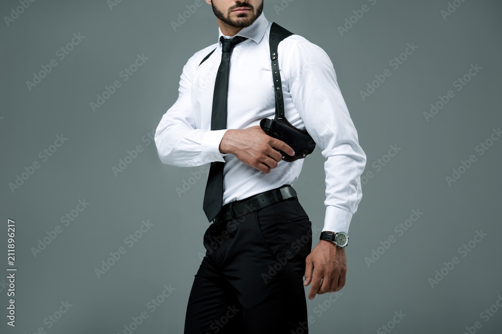 Foto de cropped image of security guard taking gun isolated on grey do ...