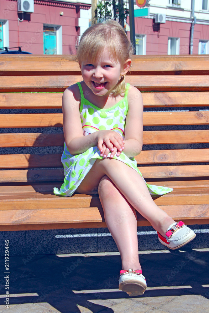 Little girl laughing while sitting on bench in city park. Positive children's emotions. Stock ...