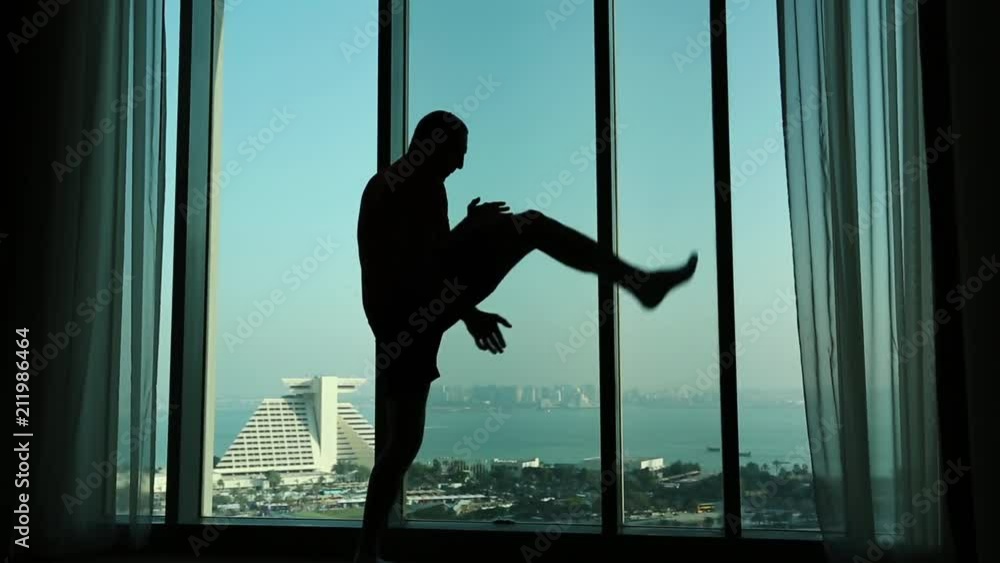 Man trains near big window in hotel room, shadow boxing. View of coast ...