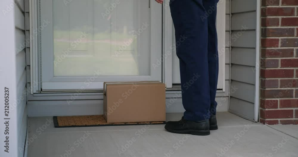 A delivery man places a cardboard box on a home's front porch then ...