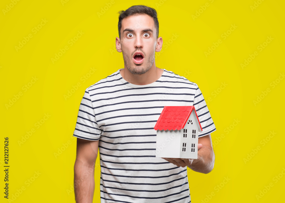 Handsome real estate agent holding a house scared in shock with a ...